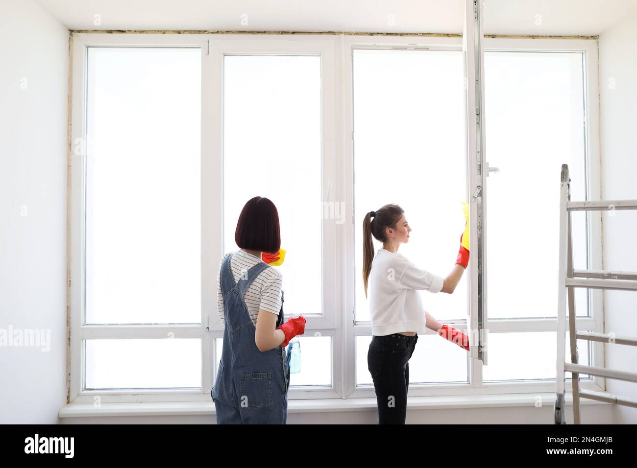 Hard working girls using spray. Young females washing window while ...