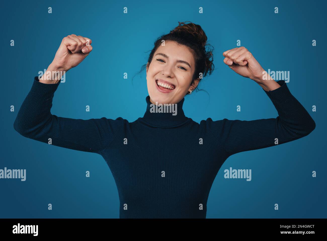 Excited young woman with raised hands and fists opening mouth and ...