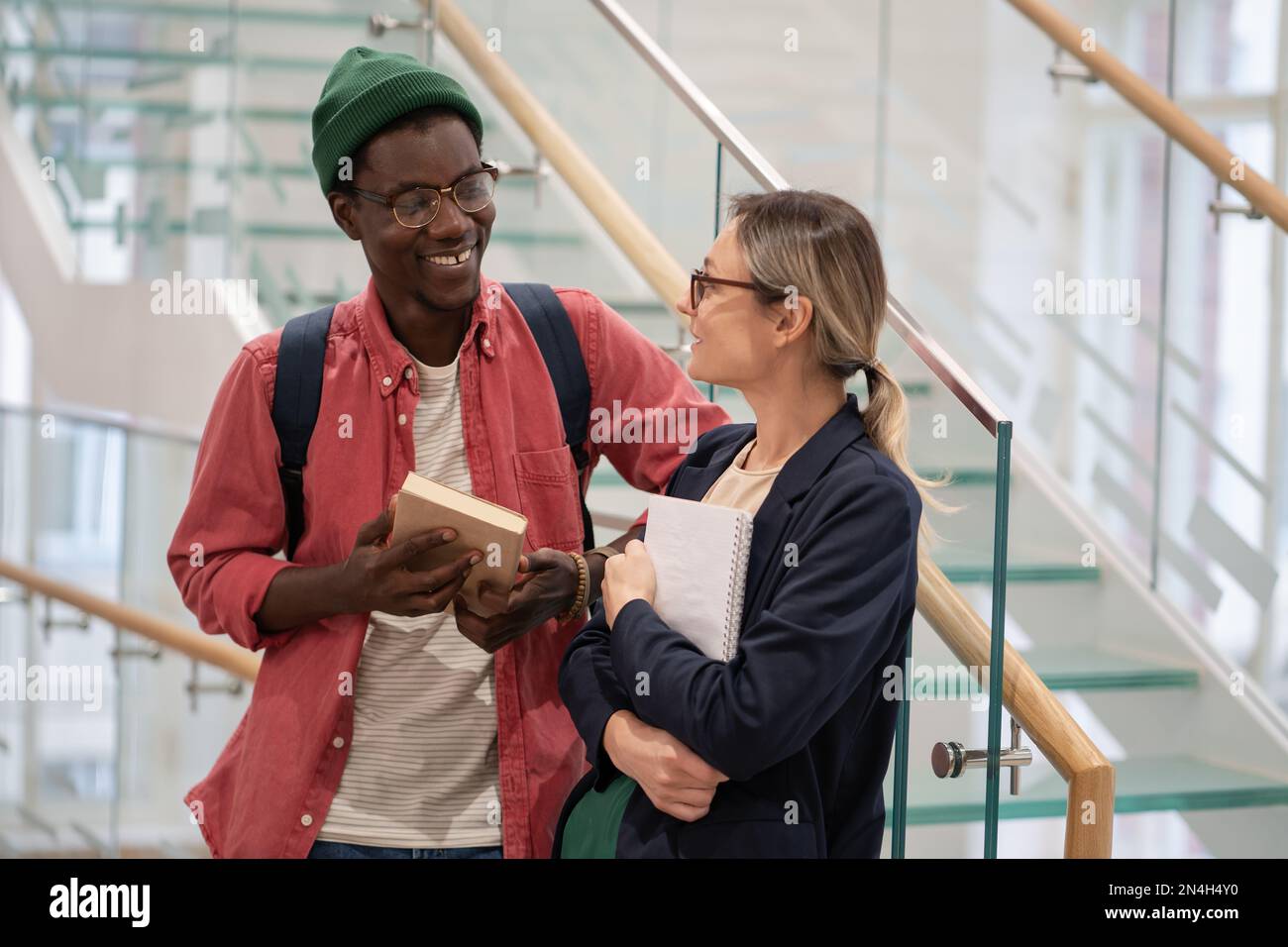 Two happy diverse students standing in university corridor talking ...