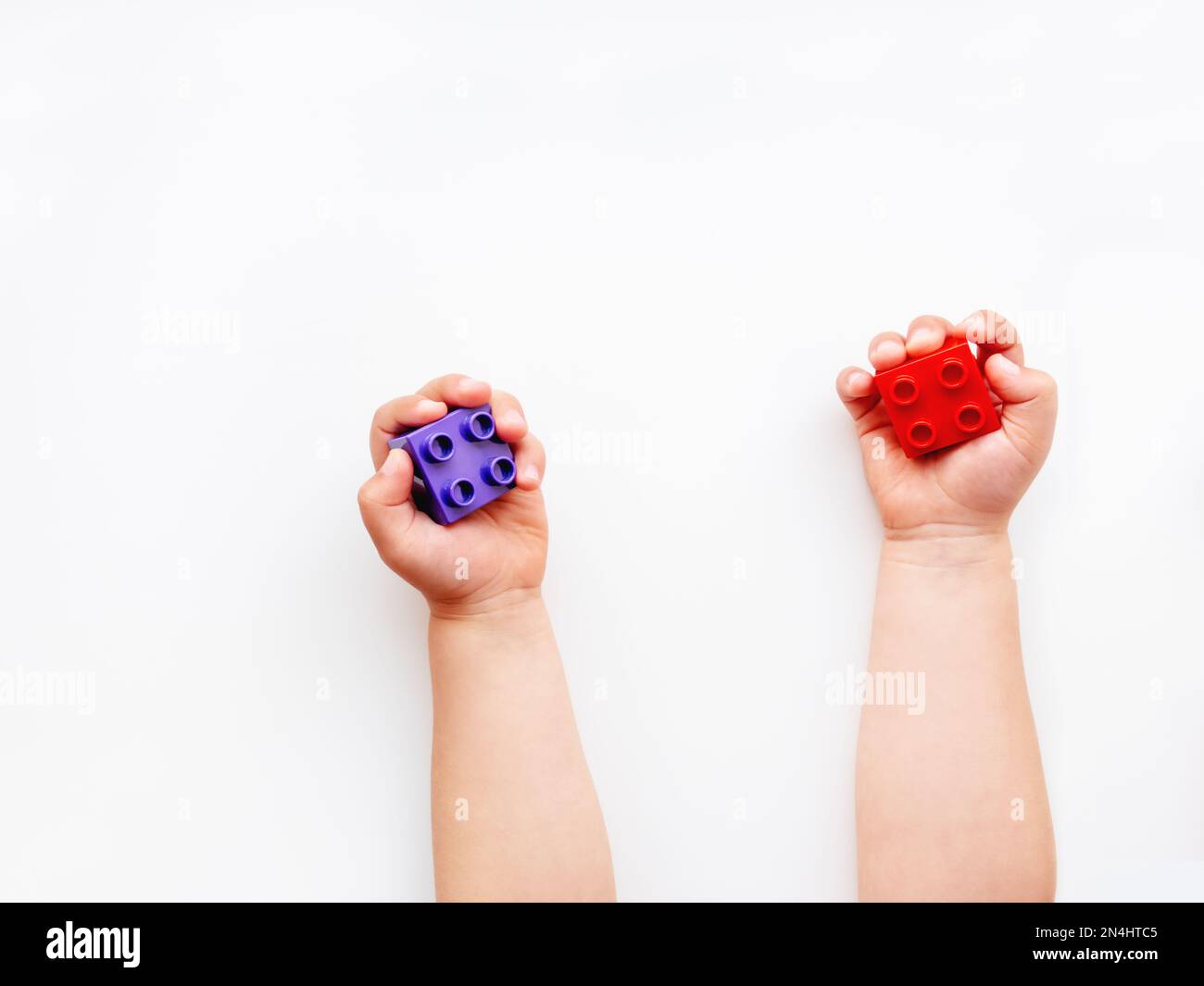 Child is holidng red and violet constructor blocks in fist. Kid's hands ...