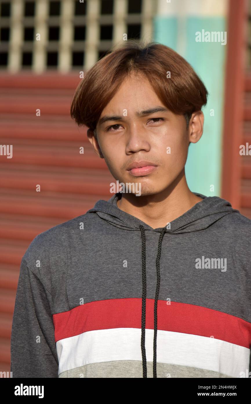 A vertical portrait of a young Southeast Asian boy with a serious ...