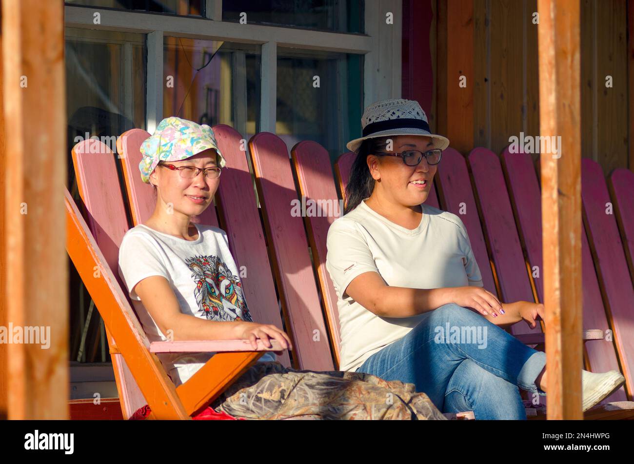 Two girls friends neighbors Asians Yakuts sitting resting in the shade ...