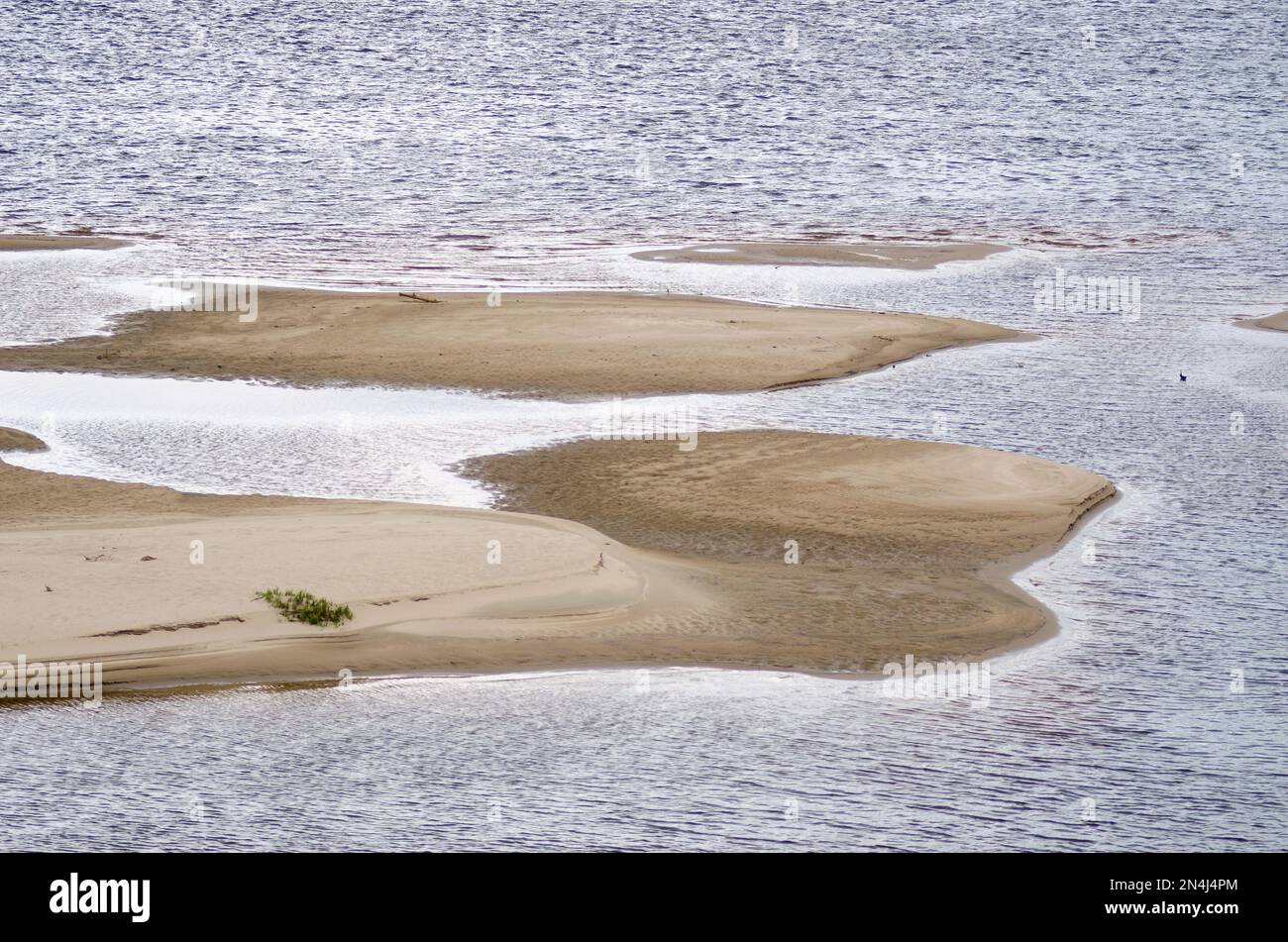 Parts of the sandy shore filled with rippling water of the river under ...