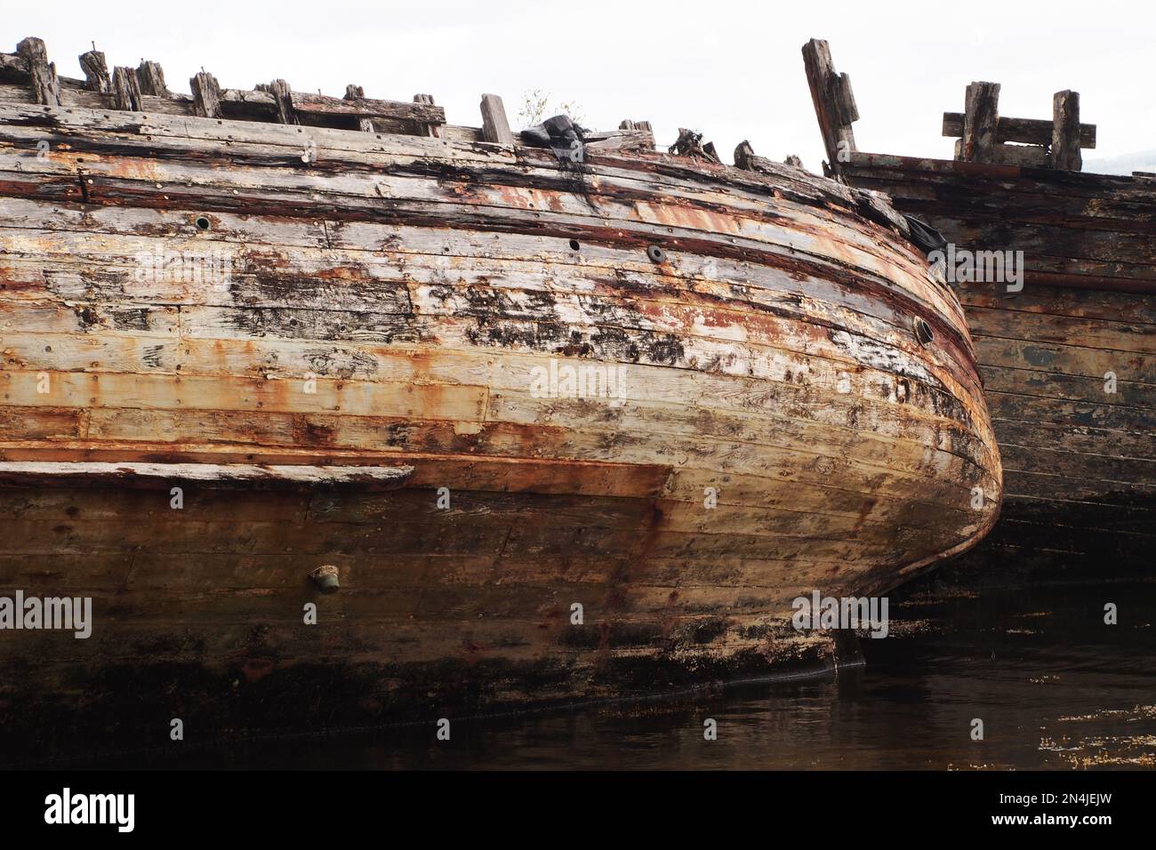 The hull of a long wooden ship leaning to one side, decaying and ...