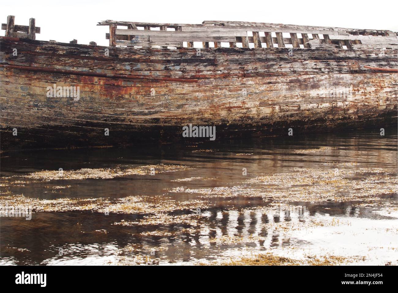 The hull of a long wooden ship leaning to one side, decaying and ...