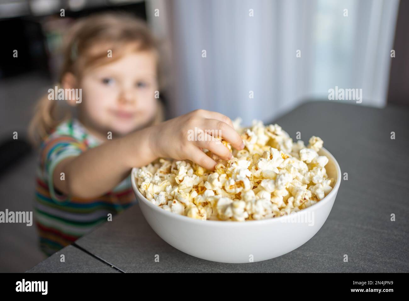 Little girl is eating popcorn in home kitchen. Focus on hand taking ...