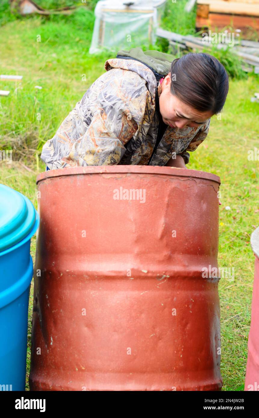 Yakut Asian girl tired washes iron tank to collect drinking rain water ...
