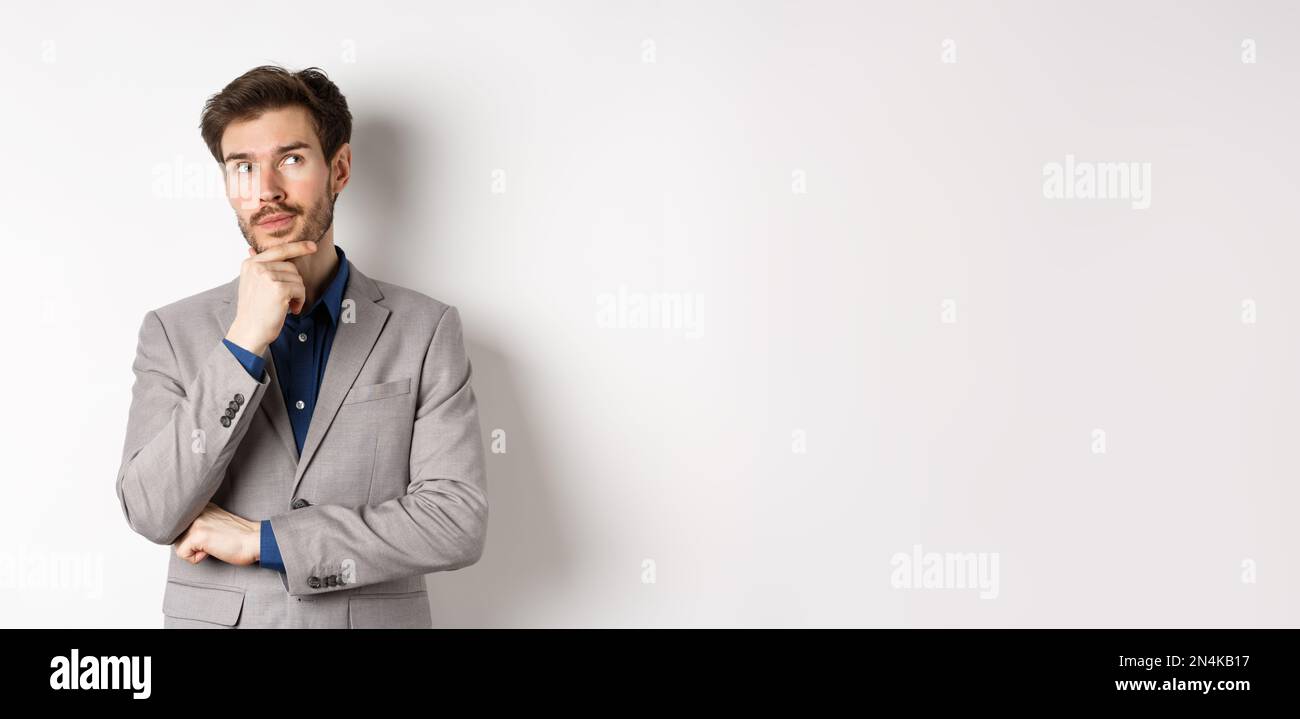Pensive handsome man in suit looking up and thinking, making choice ...