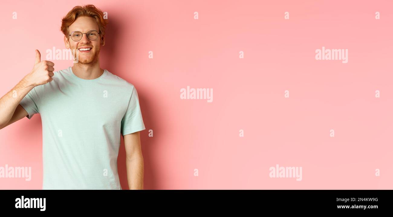 Cheerful redhead man in glasses and t-shirt, showing thumbs up with ...