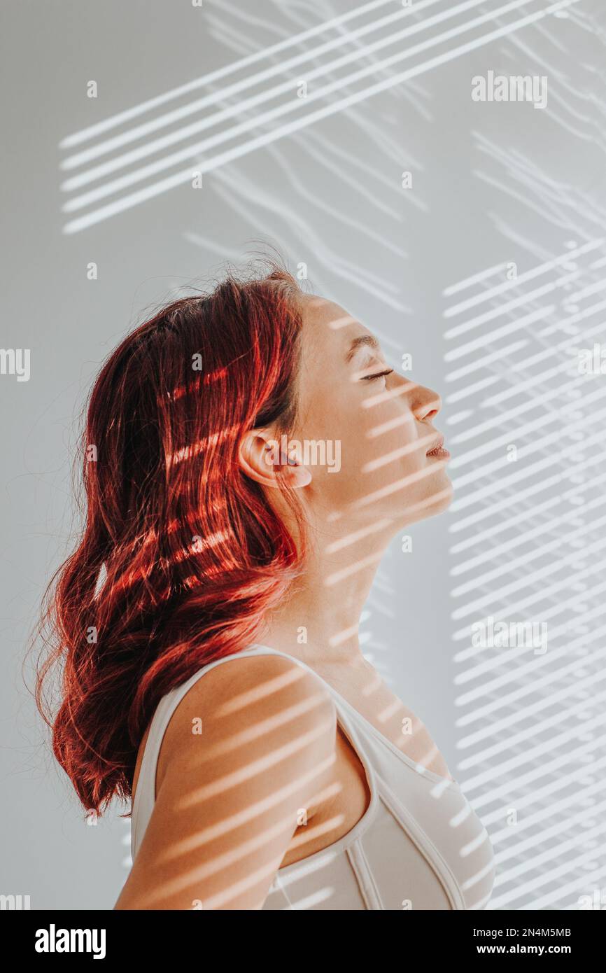 A portrait of a young red-haired female under window blinds shadows ...