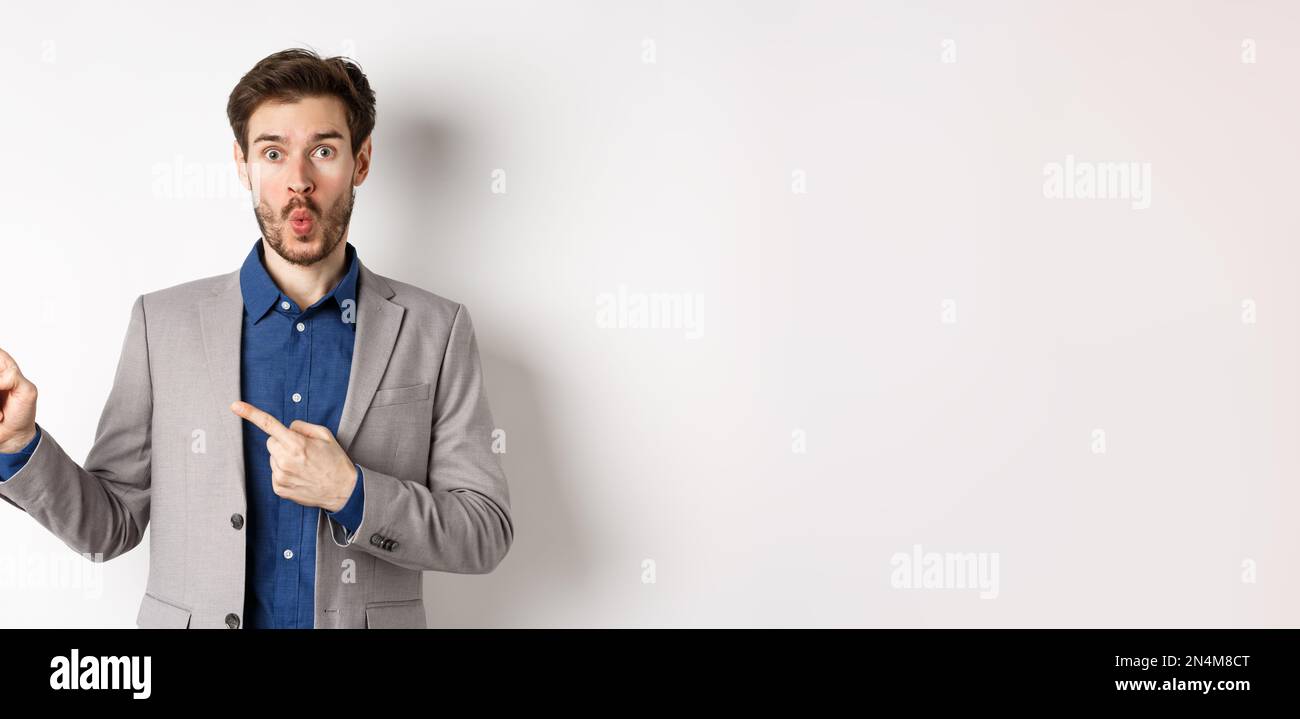 Excited handsome man in suit pointing fingers left at banner and saying ...