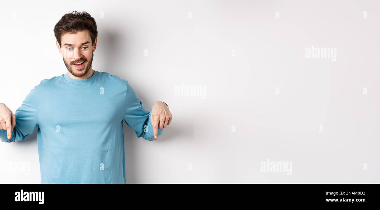 Handsome caucasian man pointing down with impressed and happy face ...