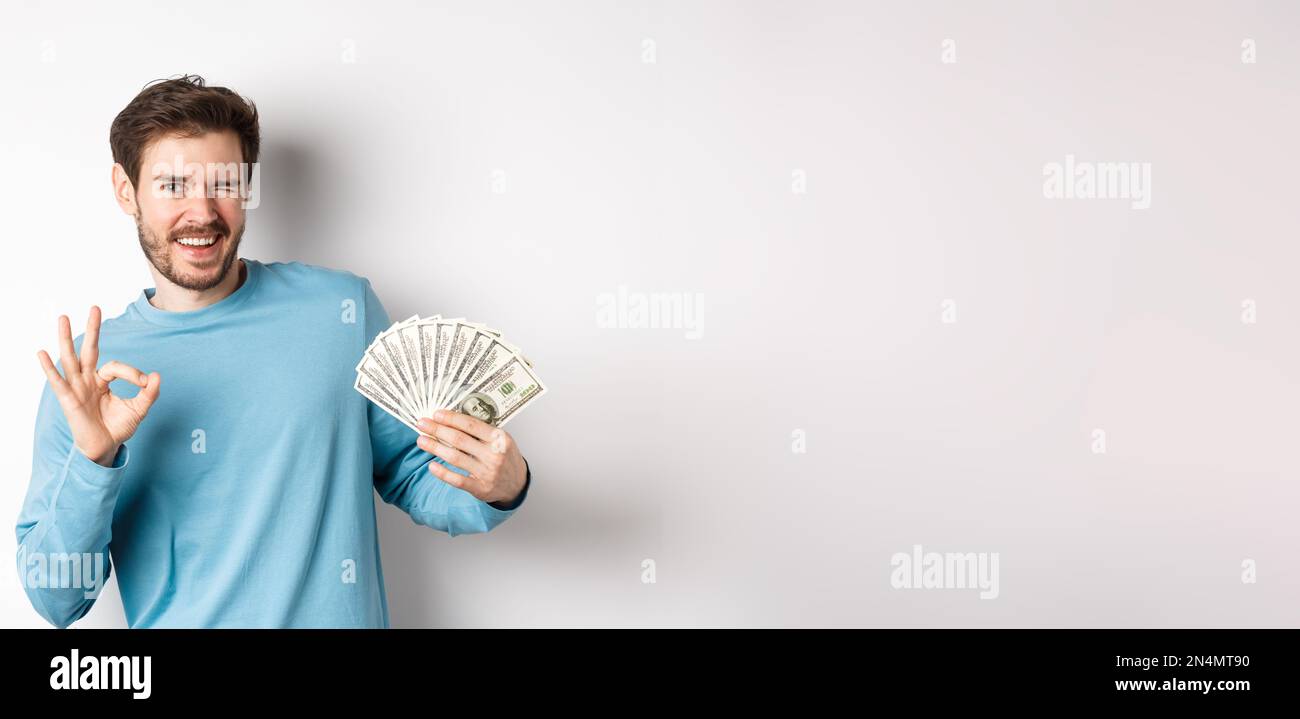 Cheeky smiling man winking, showing Ok sign and holding money, concept ...