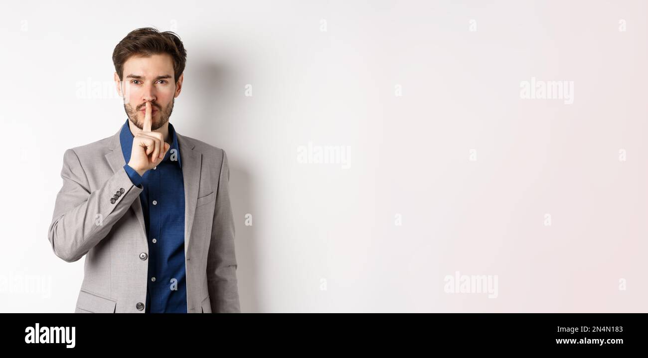 Handsome macho man in suit shushing at camera, press finger to lips ...