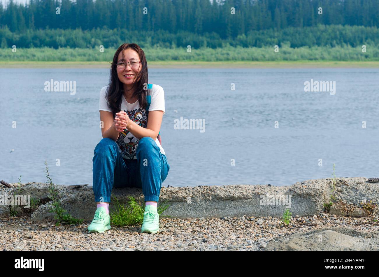 Yakut Asian young girl sitting on the stony shore, and smiling with ...