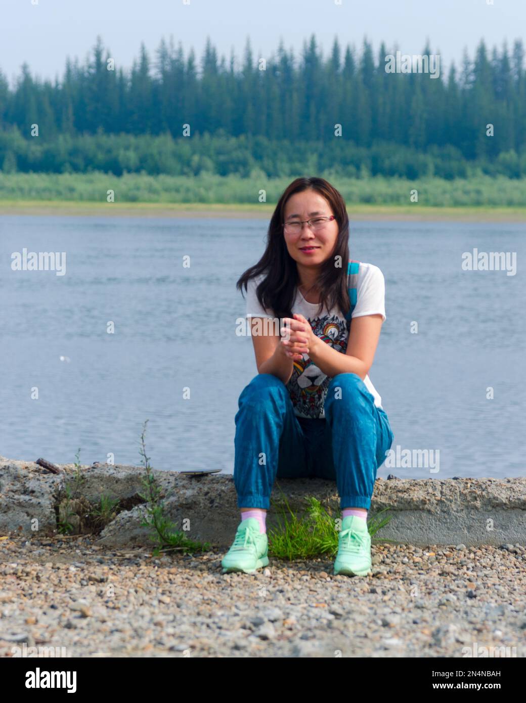 Brooding Yakut Asian young girl sitting on the stony shore, and smiling ...