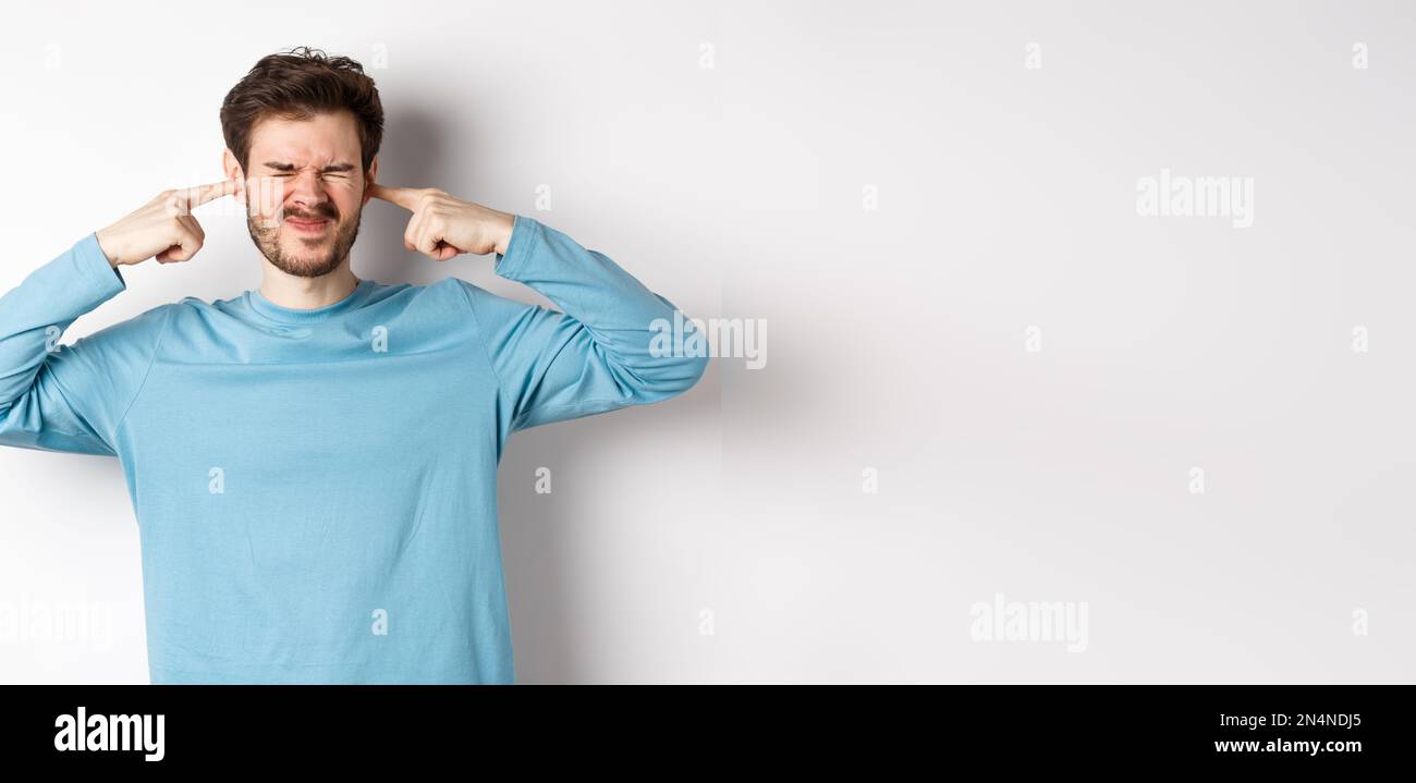 Annoyed young man plug ears from loud awful sound, being disturbed by ...