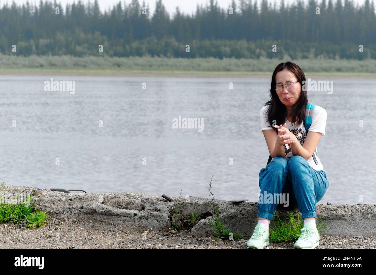 Frustrated Yakut Asian girl traveler crying on the stone Bank of the ...
