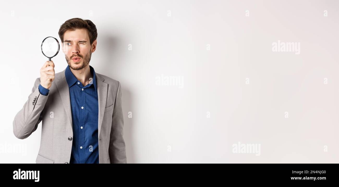Handsome male model in suit looking through magnifying glass with ...