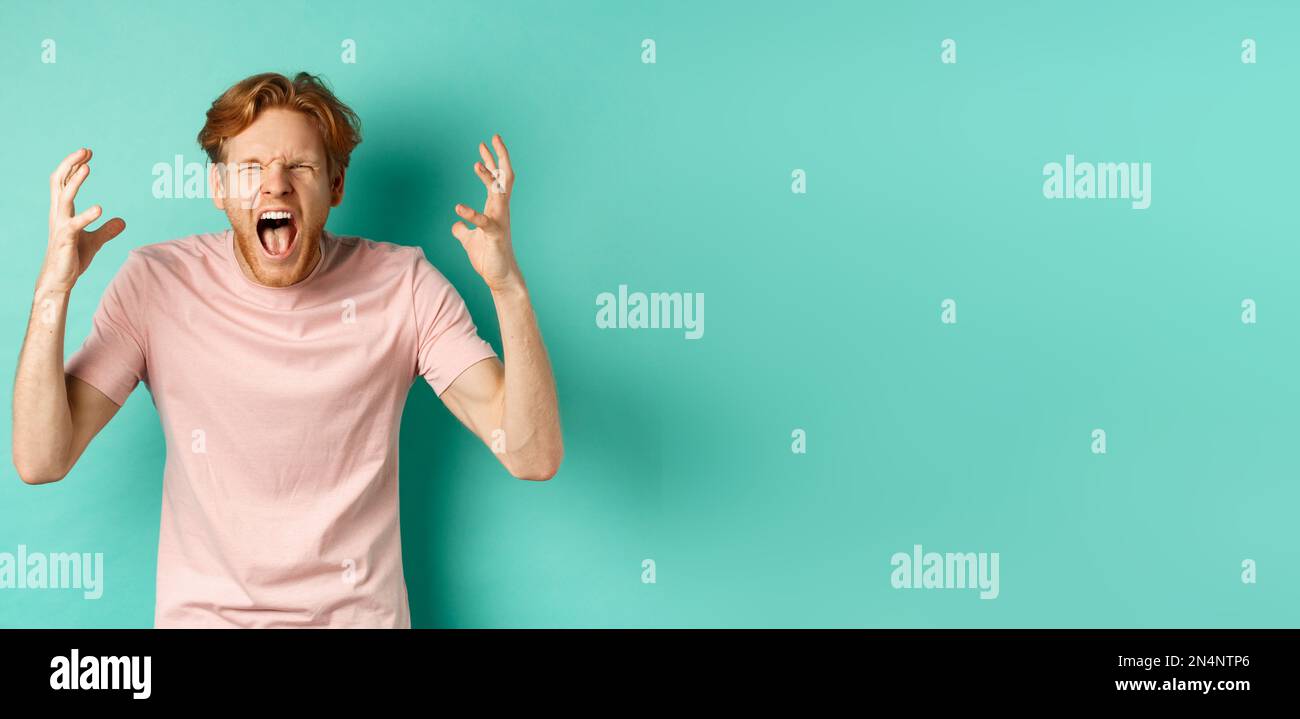 Angry young redhead man screaming distressed, shaking hands and looking ...