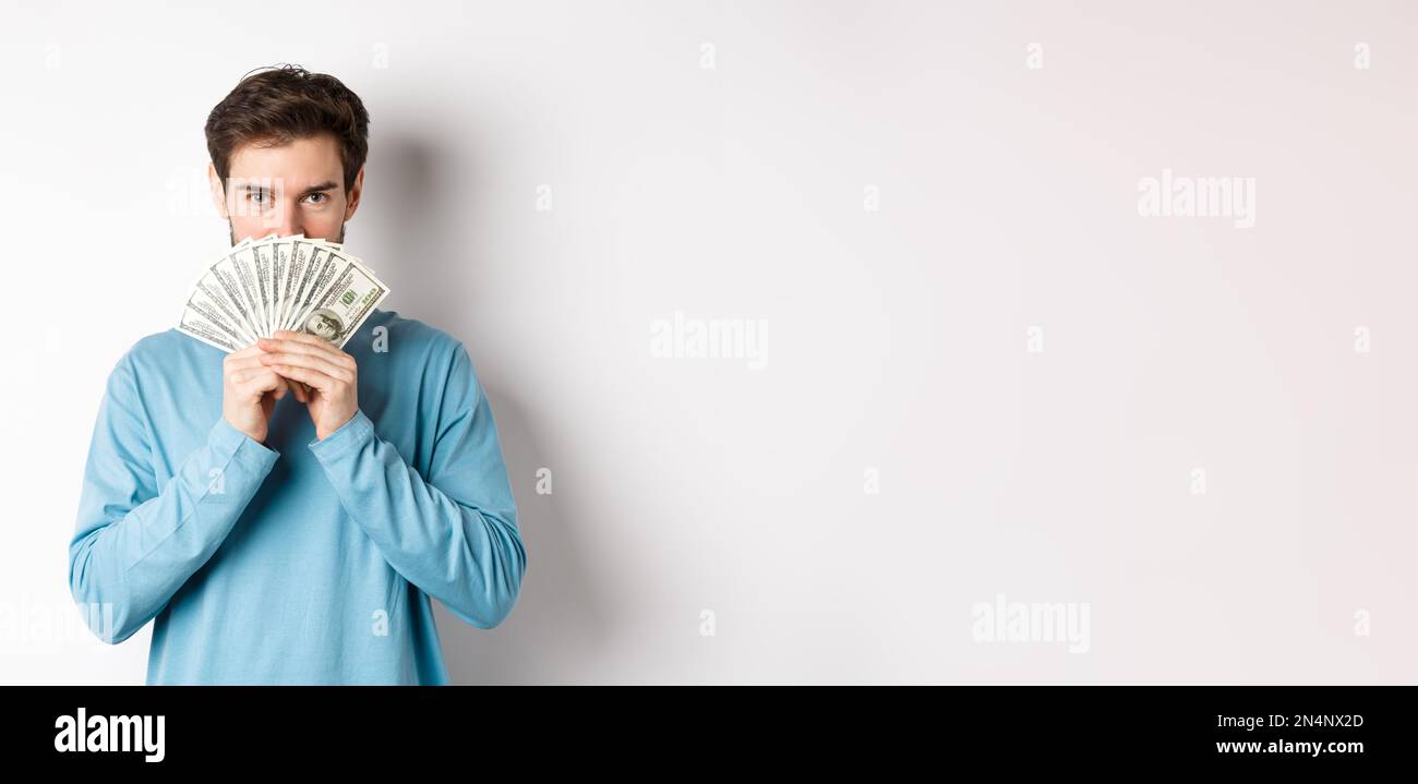 Finance concept. Smiling young man covering face behind money, showing ...