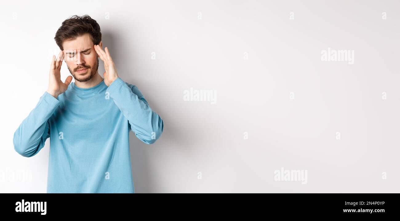 Young man having headache or hangover, touching head temples and ...
