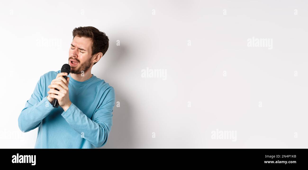 Romantic man singing song in microphone at karaoke, standing over white ...