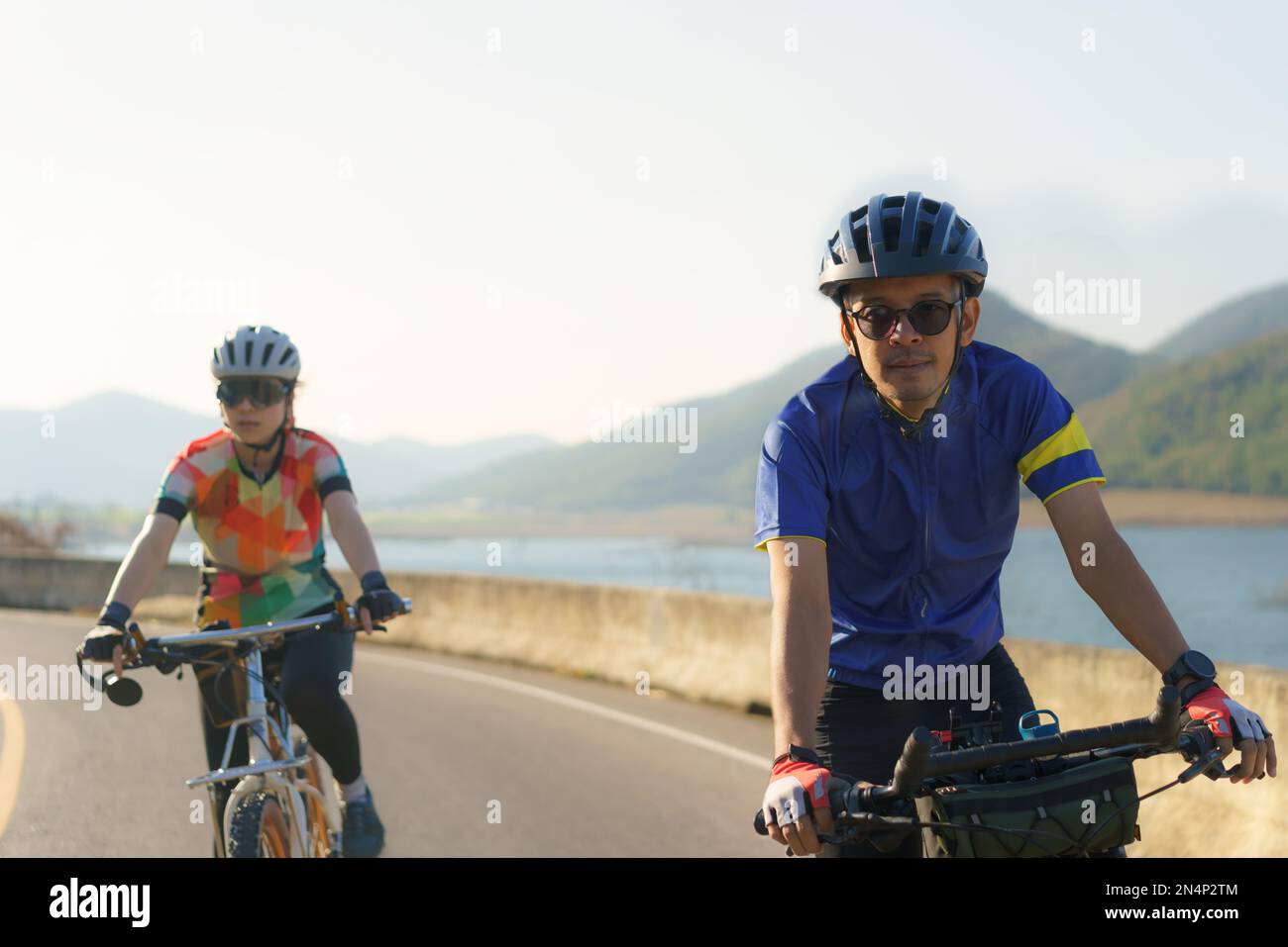 Asian cyclist couple riding together for exercise around the lake in ...