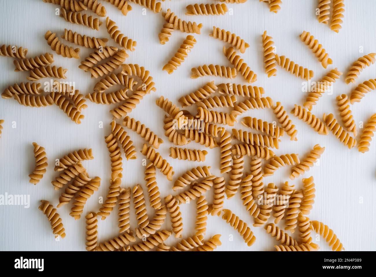 Flat lay of scattered many wavy pasta from whole wheat flour on white ...