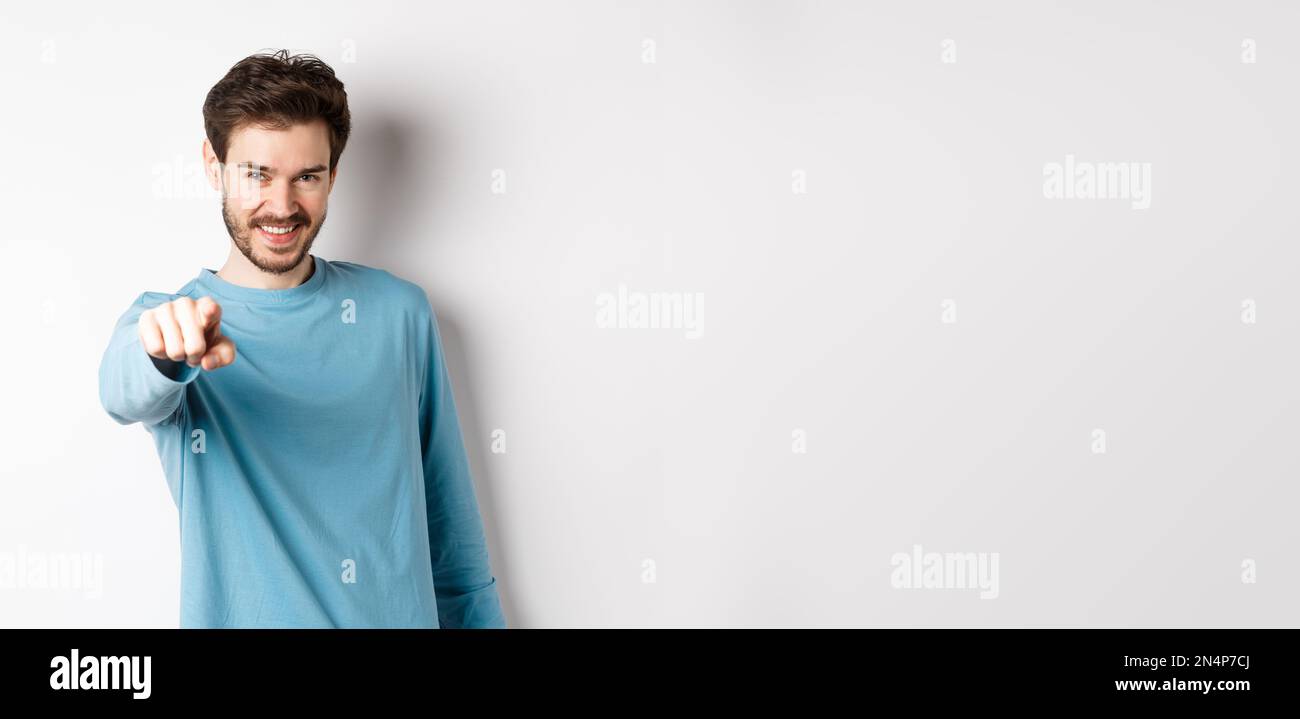Image of confident young man smiling and pointing at camera, inviting ...