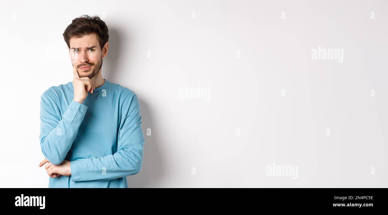 Skeptical young man frowning, looking with worried thoughtful look ...