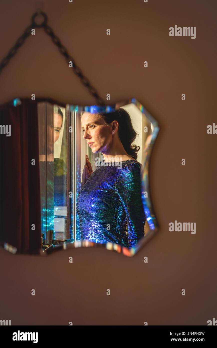 Reflection in a wall mounted mirror of a woman looking thoughtful ...