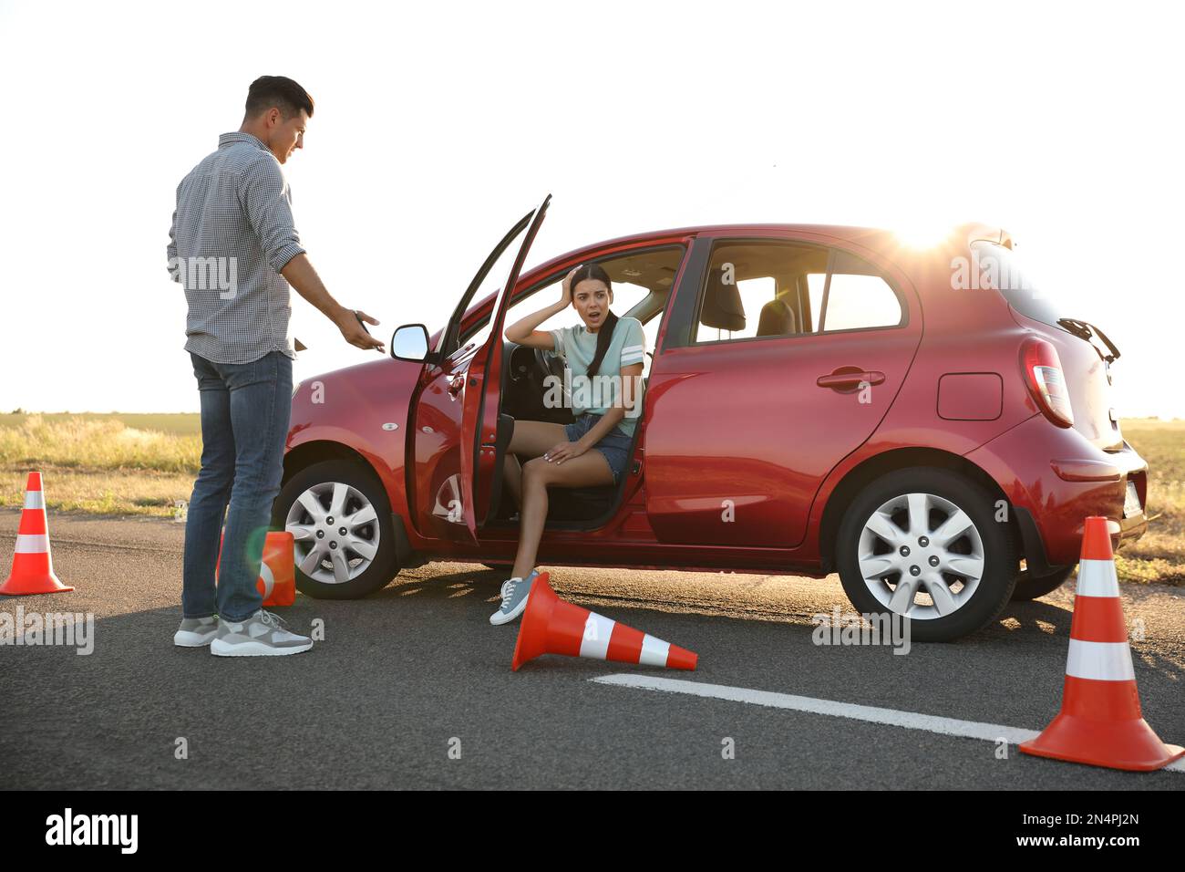 Stressed young woman in car near instructor and fallen traffic cones ...