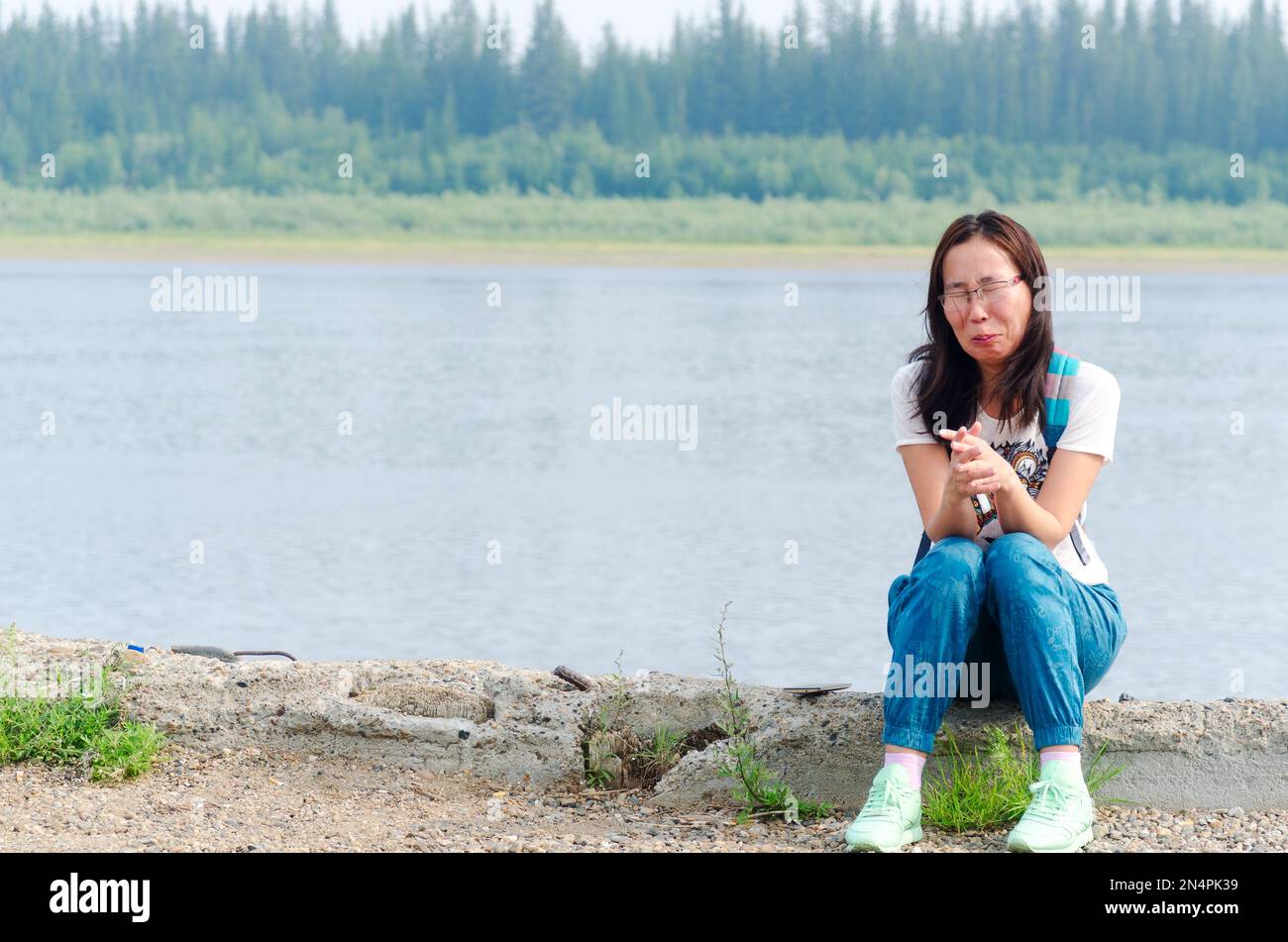 Frustrated Yakut Asian girl traveler crying with folded hands on the stone Bank of the Northern ...
