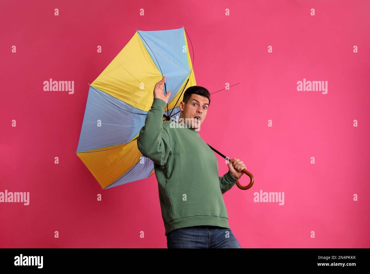 Emotional man with umbrella caught in gust of wind on pink background ...