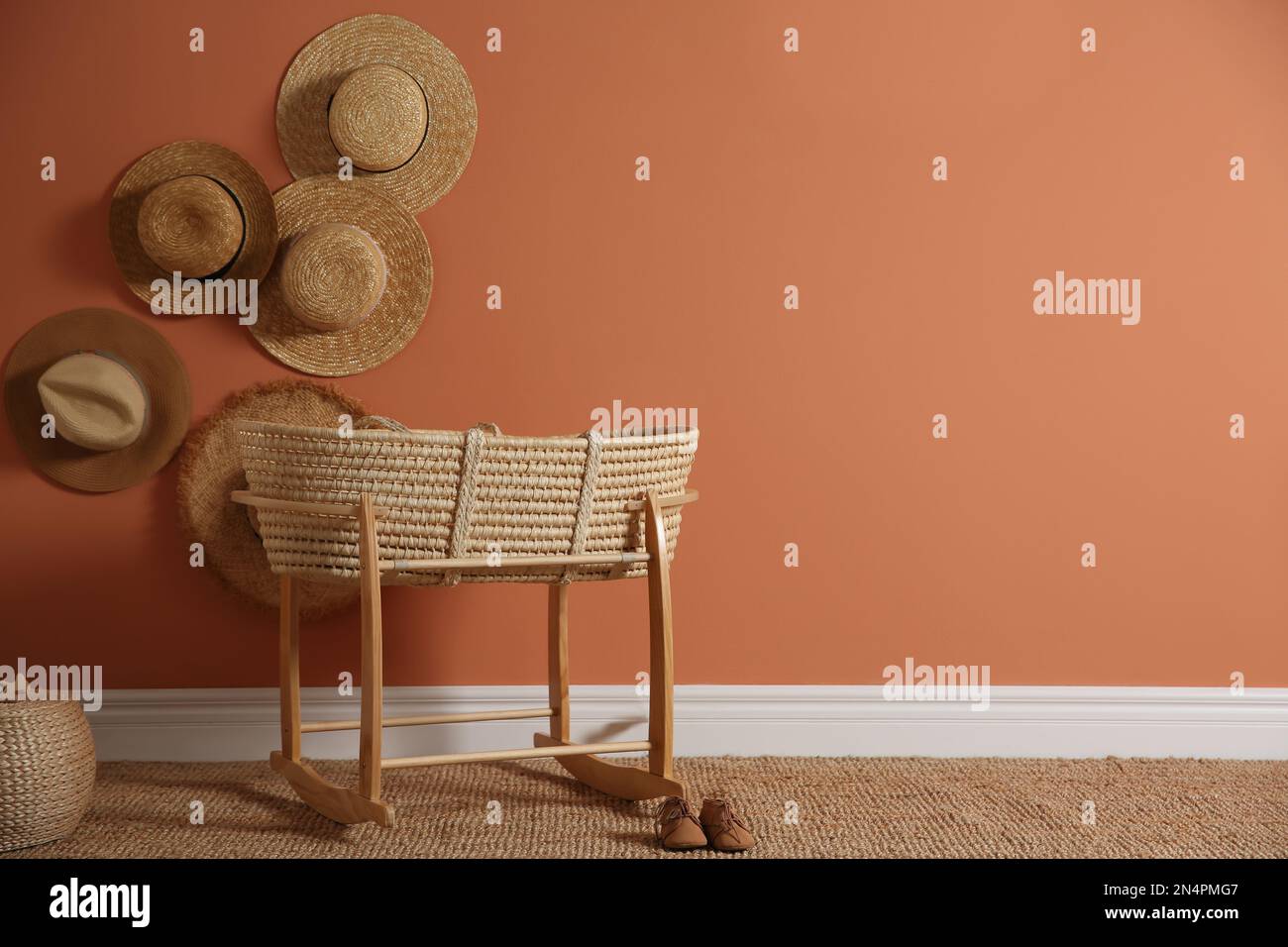 Wicker crib and straw hats on brown wall, space for text. Interior ...