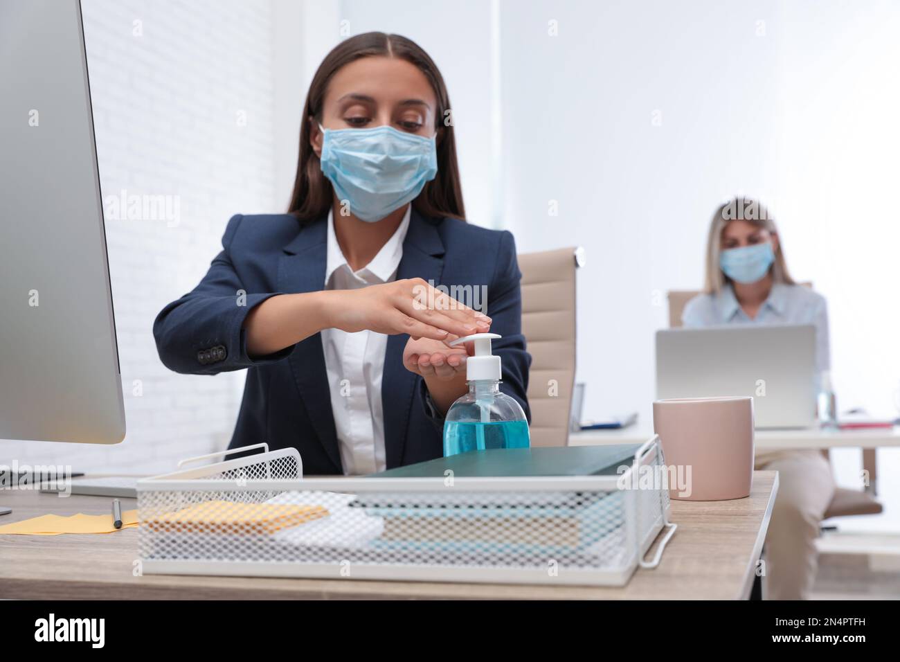 Office employee in mask applying hand sanitizer at workplace Stock ...
