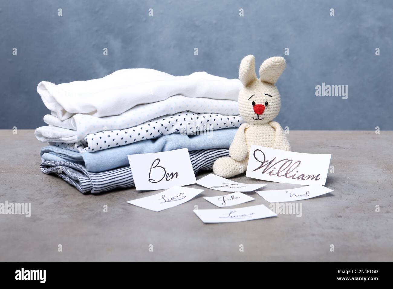 Paper sheets with different baby names, toy and child's clothes on grey ...