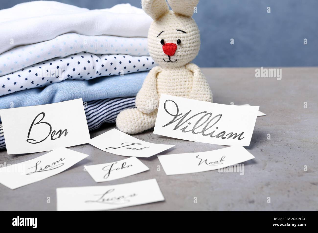 Paper sheets with different baby names, toy and child's clothes on grey ...