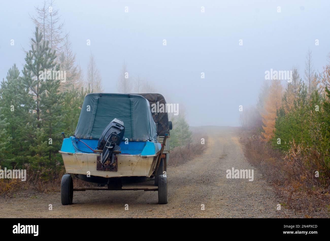 A boat on a trailer with a motor is on the road in the spruce taiga in ...