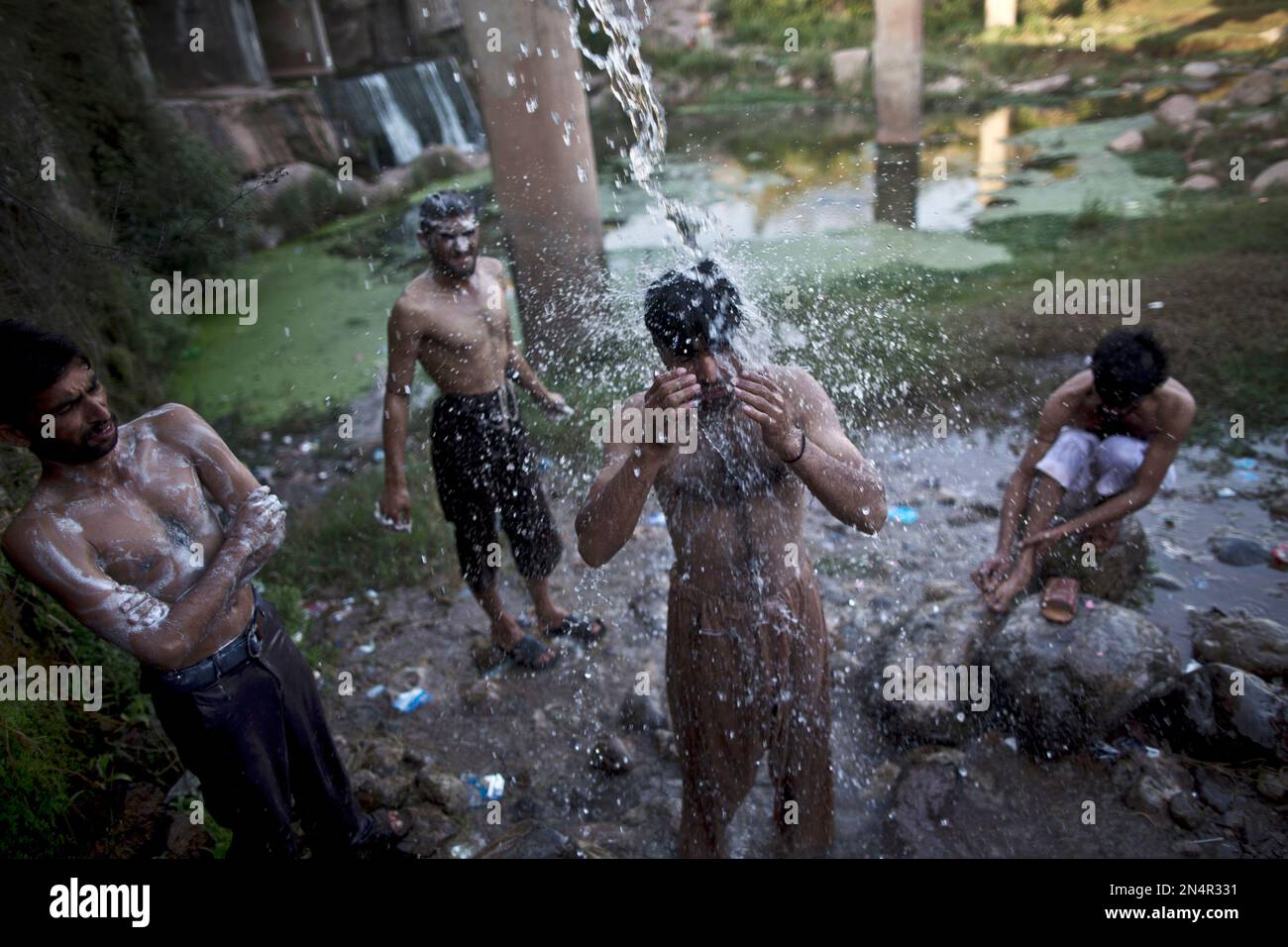 Pakistani day laborers shower under a leaking water supply pipe ...