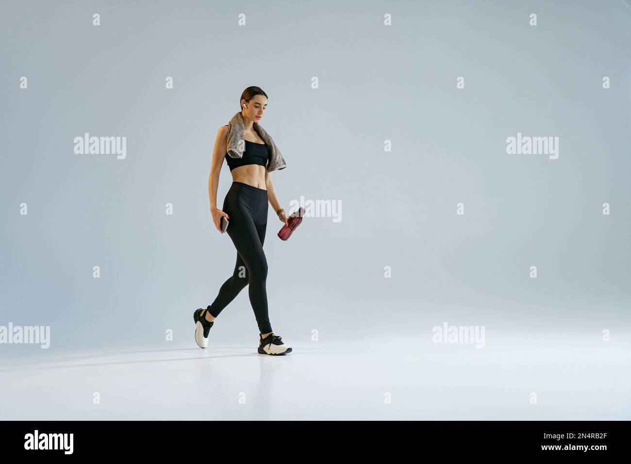 Woman walking with water bottle and towel around her neck over studio background Stock Photo - Alamy