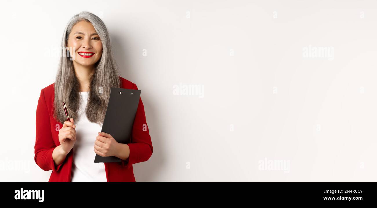 Successful asian lady boss in red blazer, holding clipboard with ...
