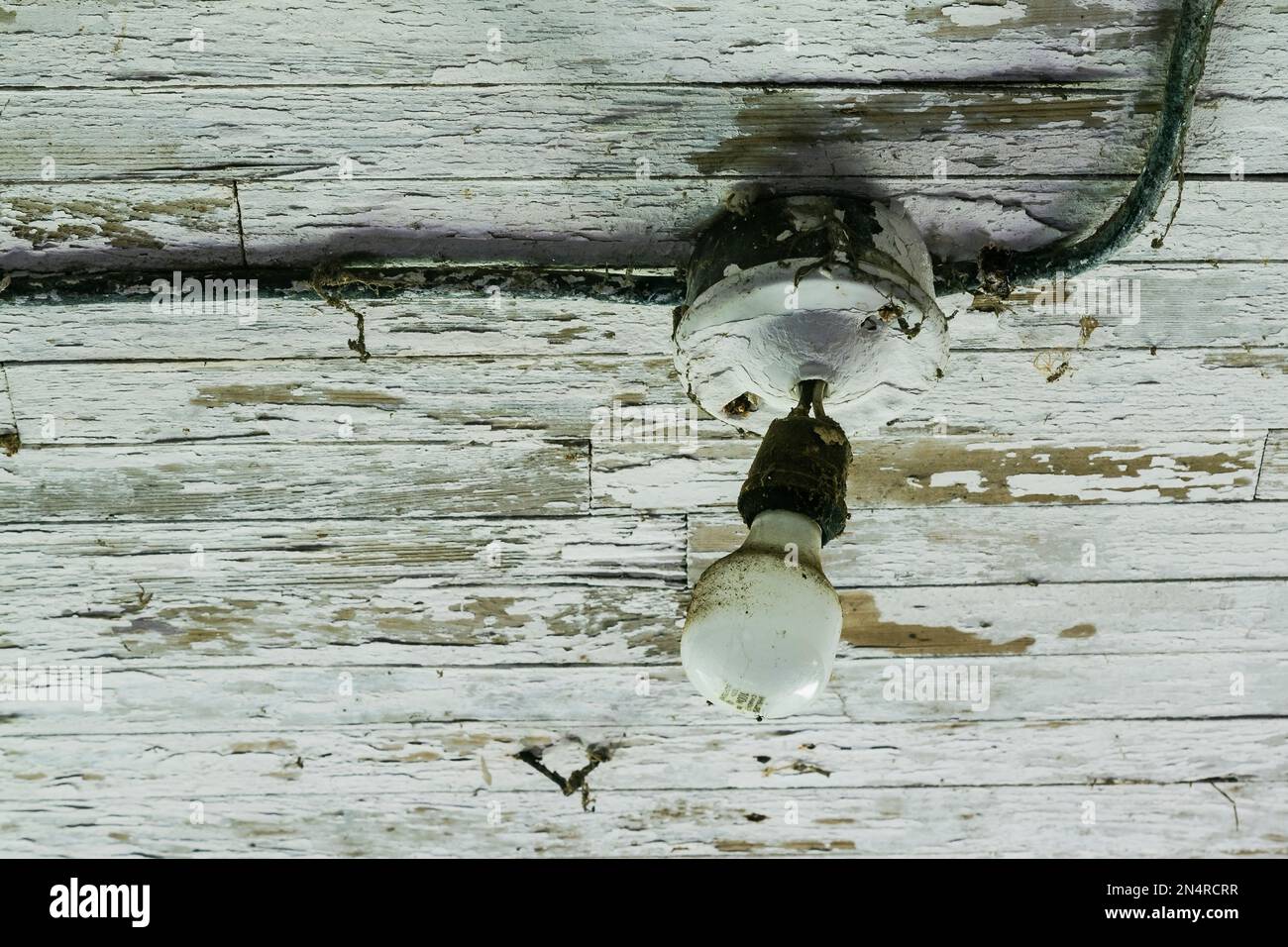 Close-up of dangling light bulb and faded white painted wood planked ...