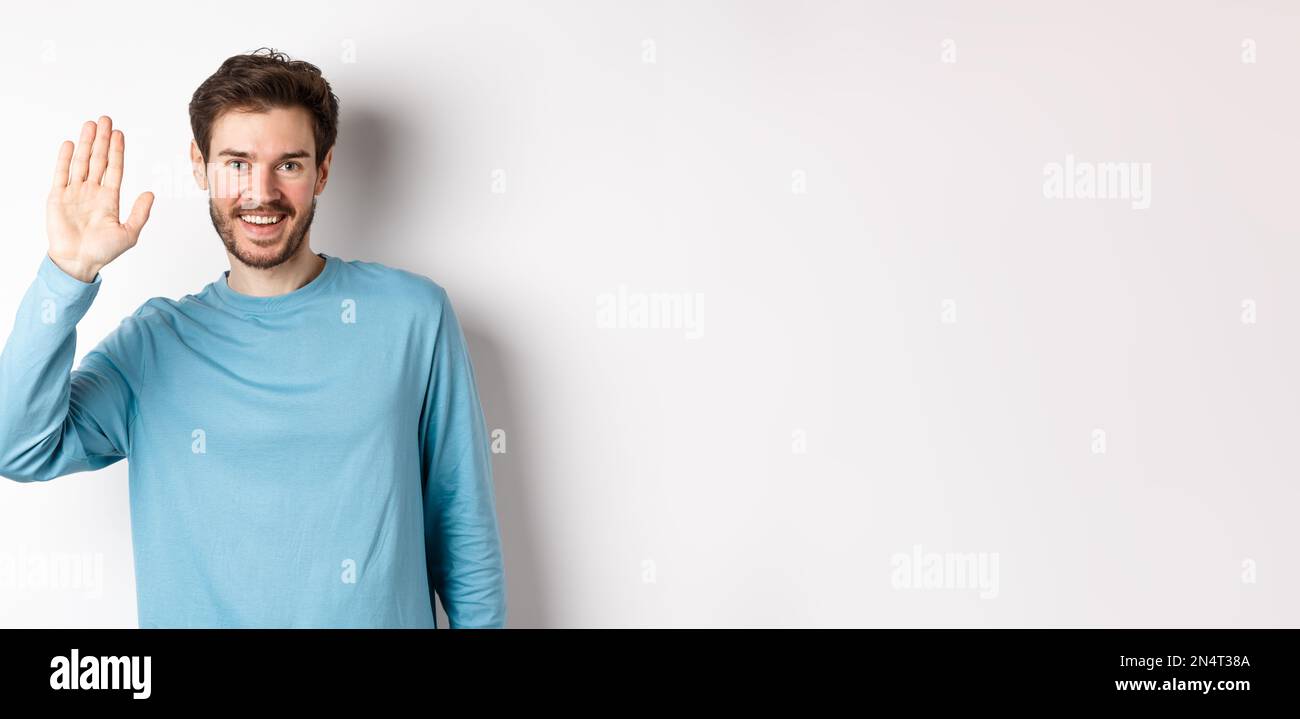 Cheerful young man with beard saying hello, looking friendly and waving ...