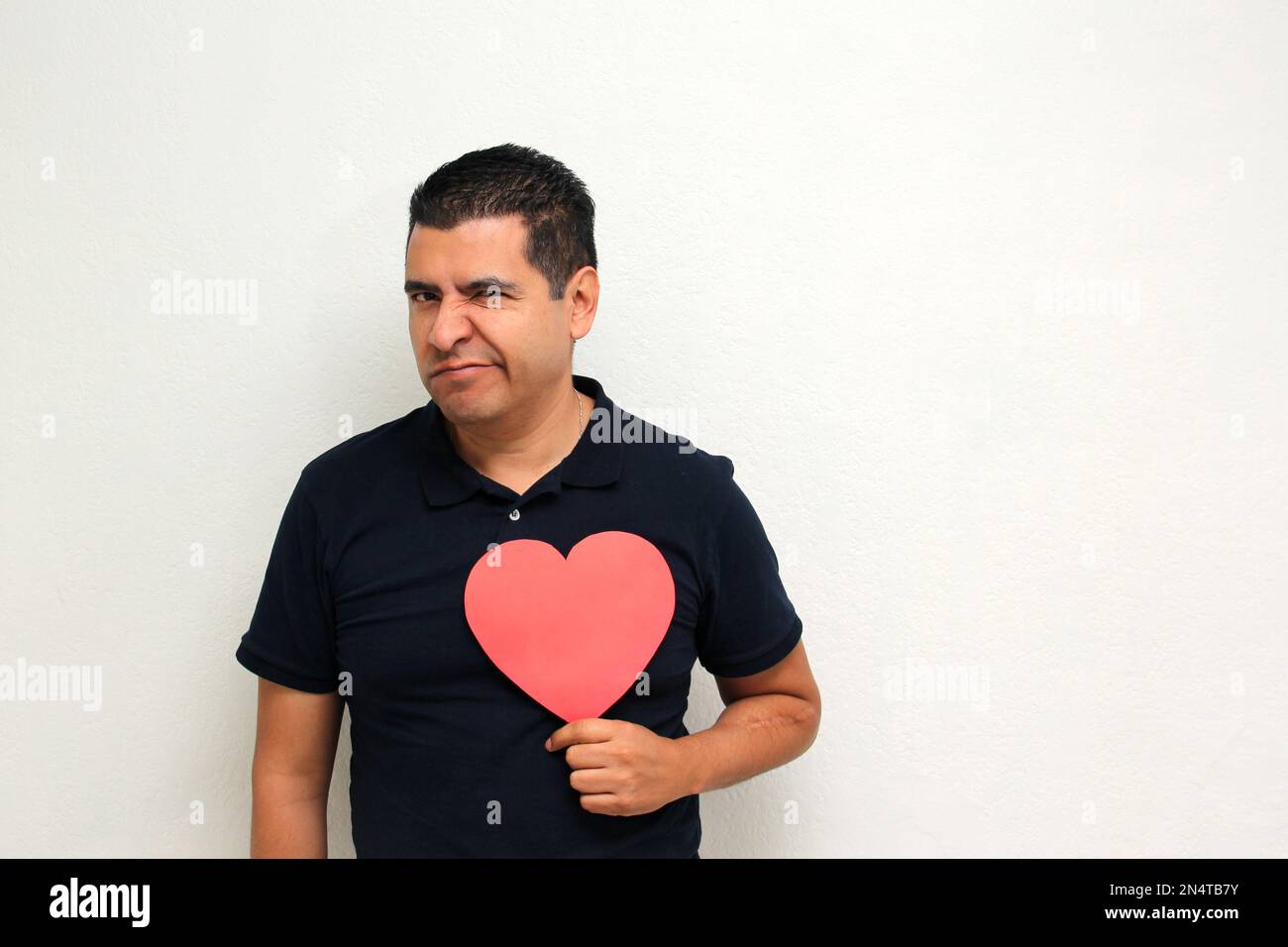Latino adult man with a big red heart shows his anger, disgust, sadness ...