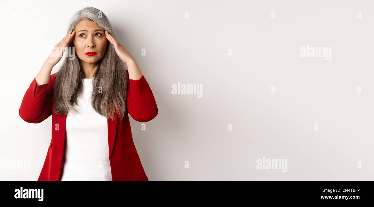 Troubled asian office woman touching head, looking aside and looking ...