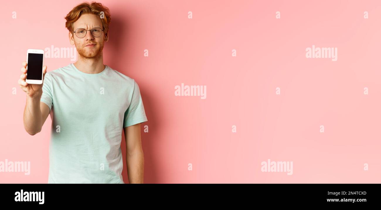 Disappointed male model frowning, showing smartphone screen, standing ...