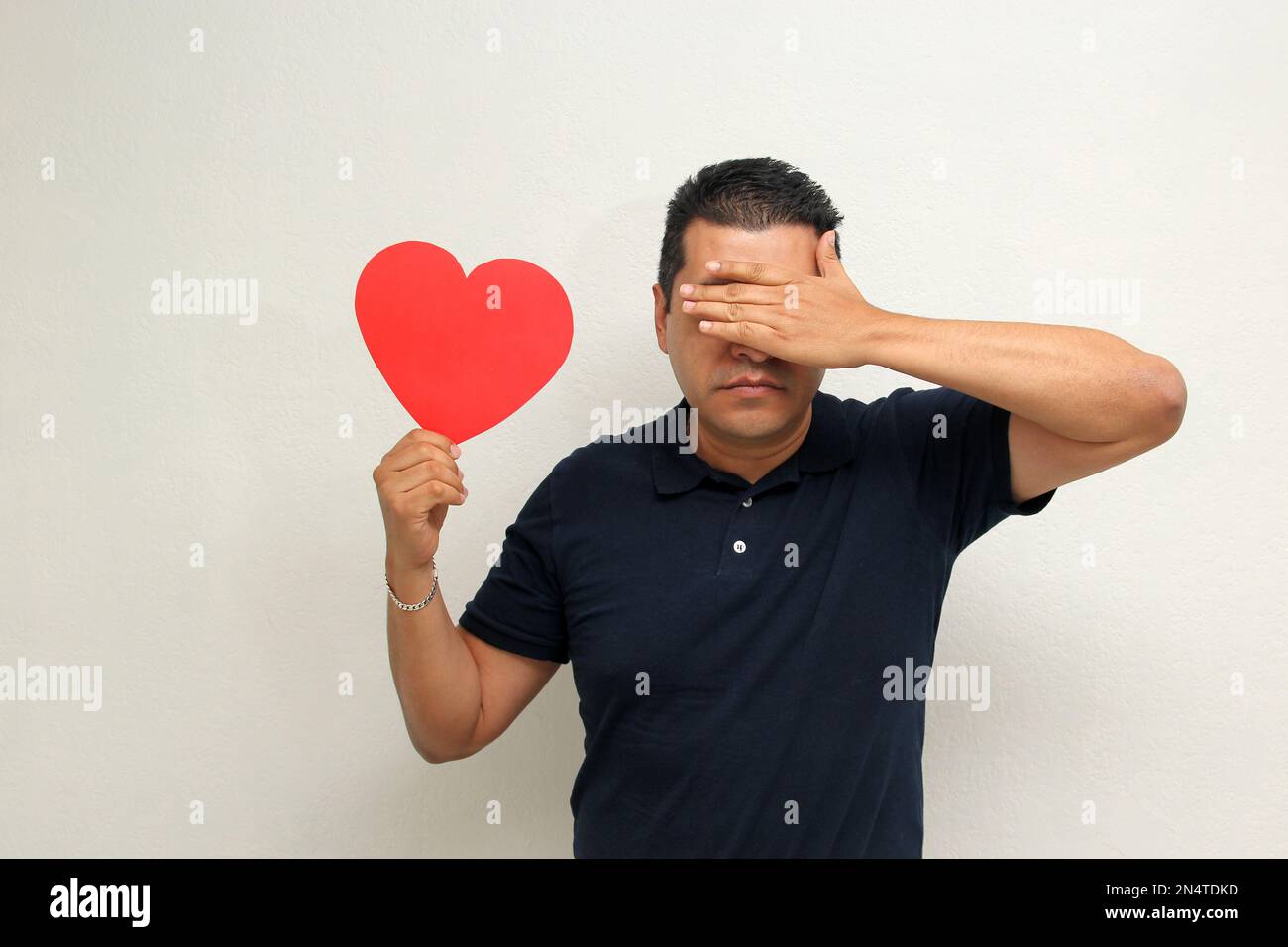 Latino adult man with a big red heart shows his anger, disgust, sadness ...