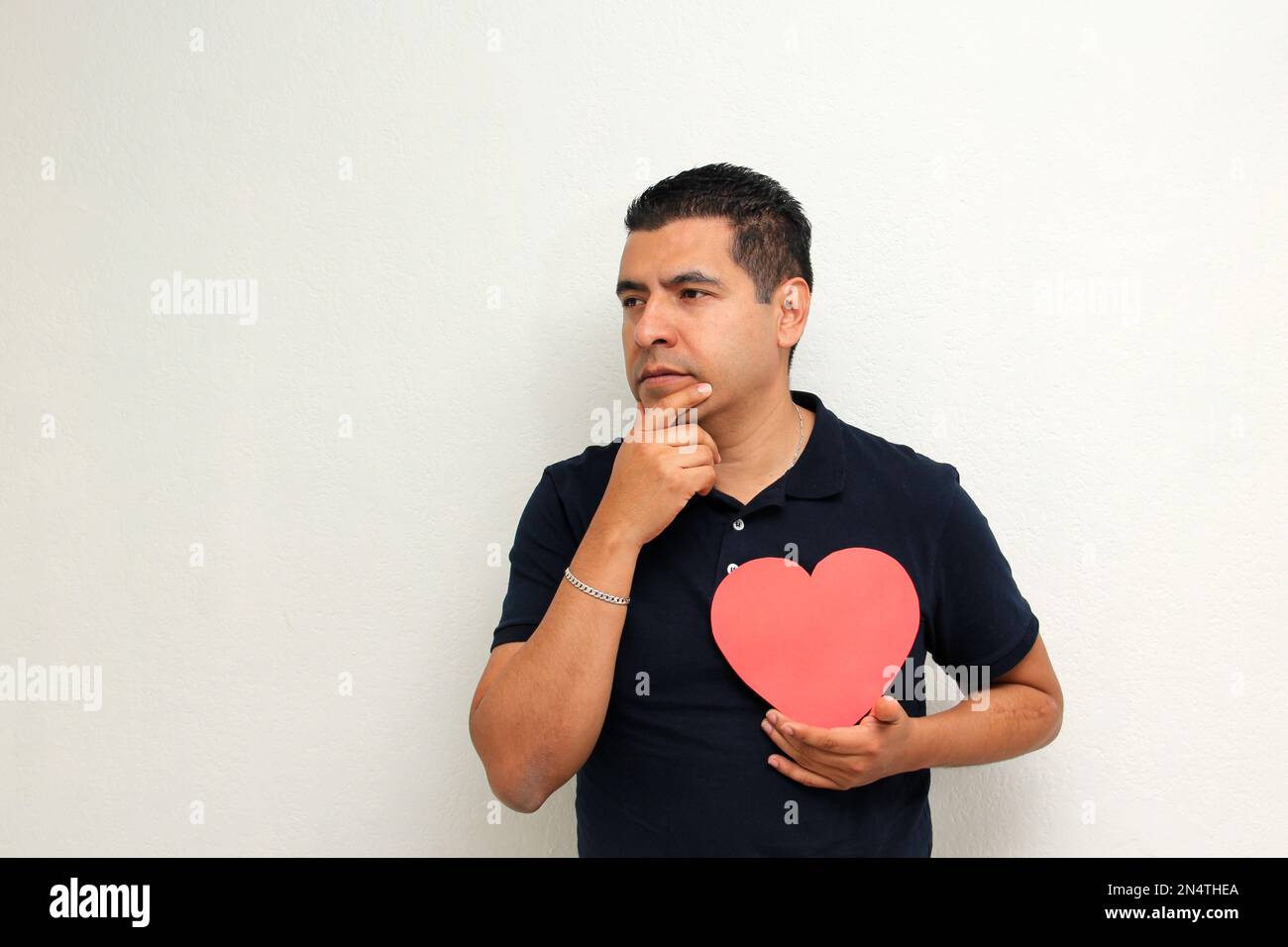 Latino adult man with a big red heart shows his anger, disgust, sadness ...